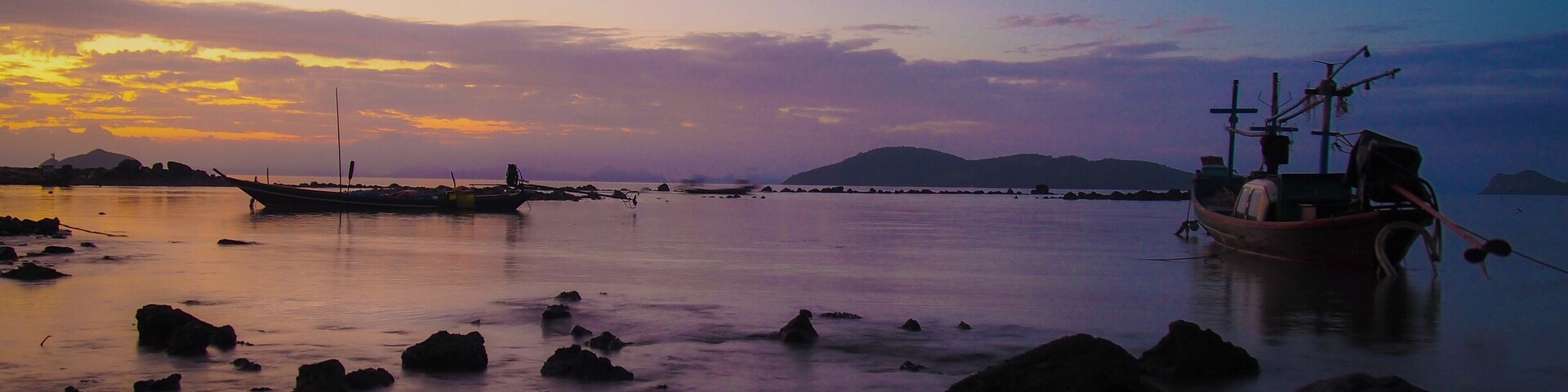 Cena costeira tranquila com barcos ancorados perto de rochas ao pôr do sol.
