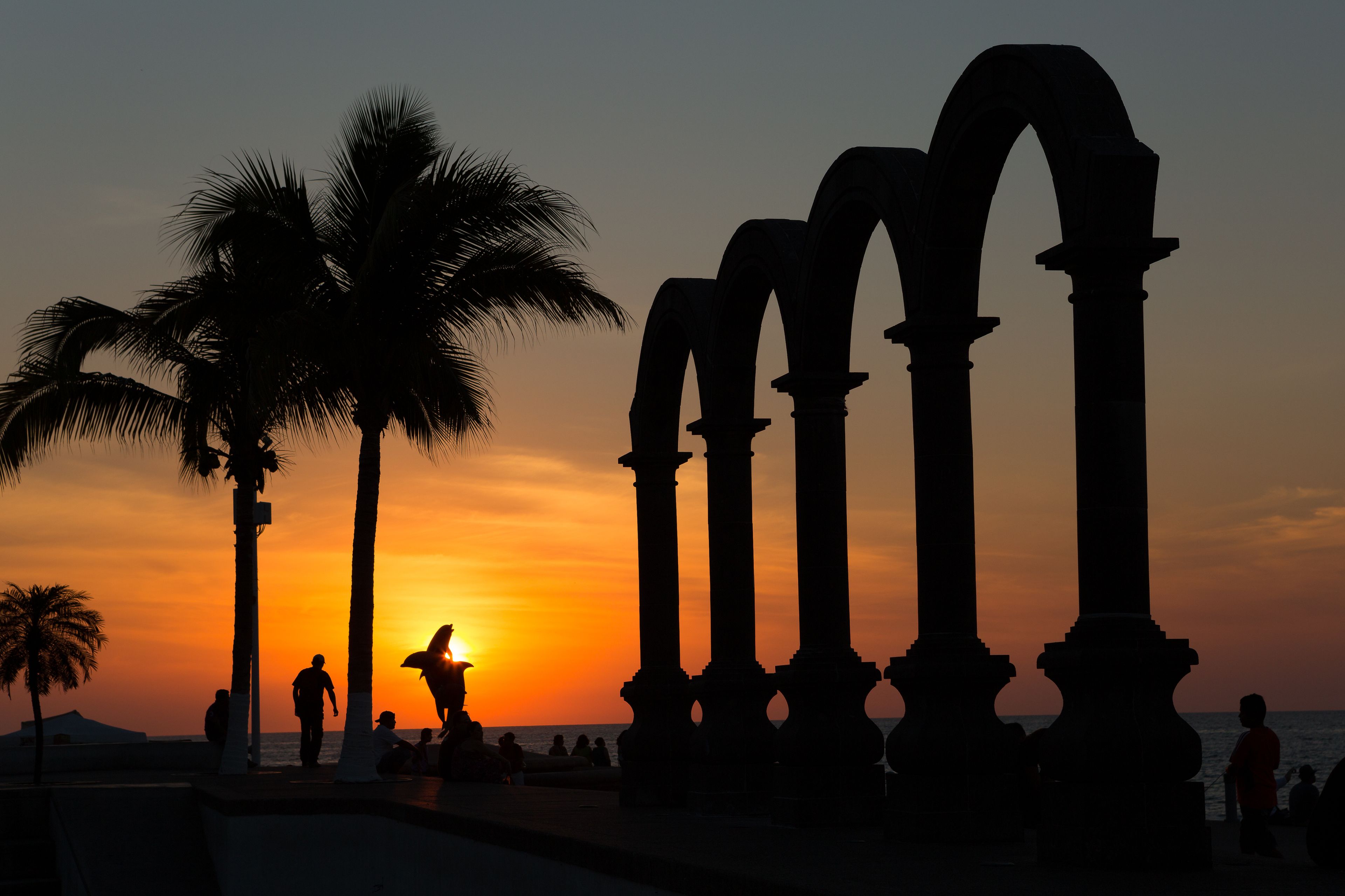 Pôr do sol com silhuetas de palmeiras e colunas clássicas.