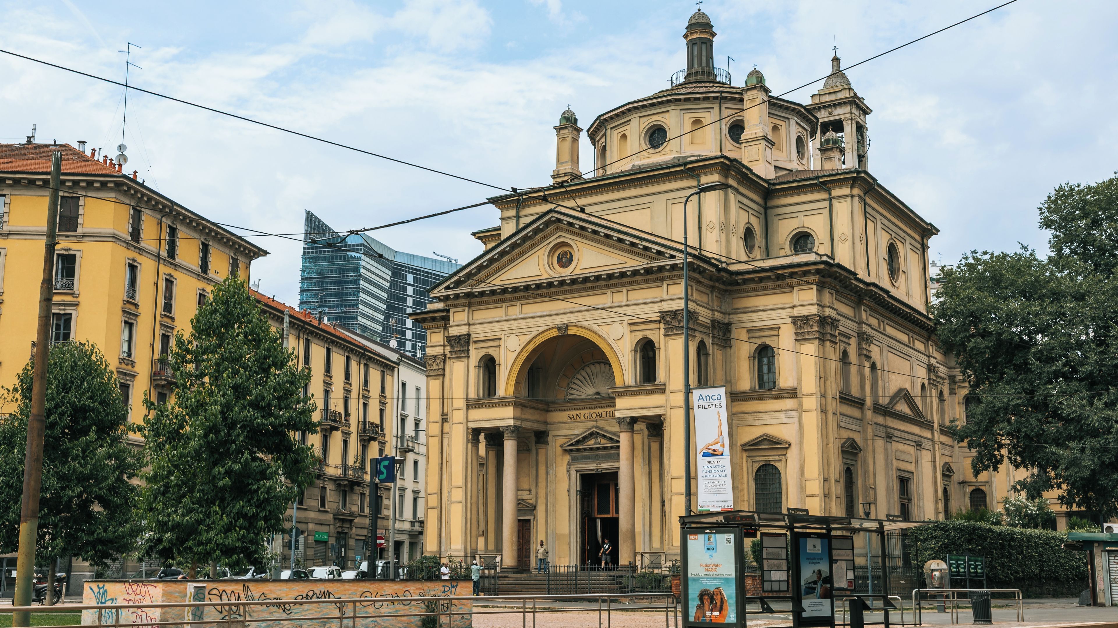 Uma igreja histórica com uma cúpula imponente e um campanário, cercada por edifícios modernos e árvores.