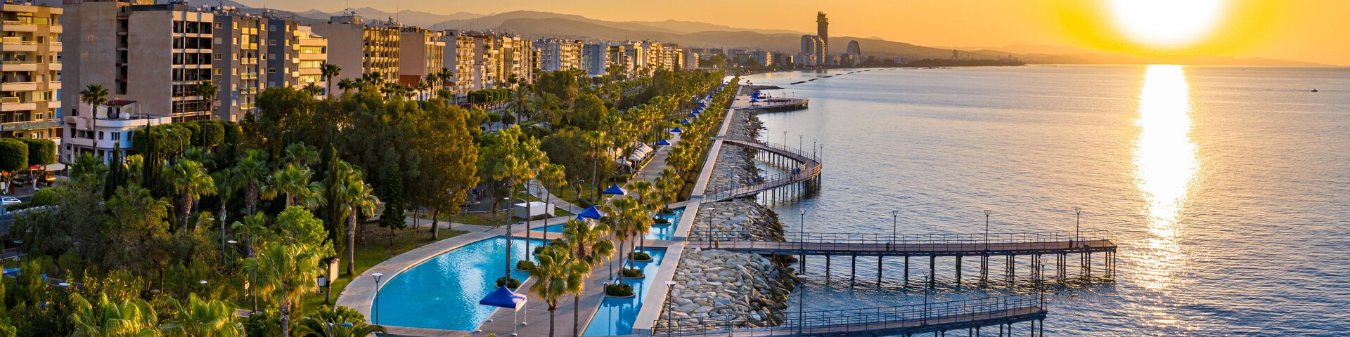 Resort à beira-mar com piscina, palmeiras e um píer que se estende sobre a água.