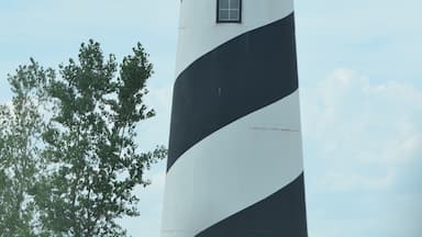 Um farol com listras pretas e brancas, um telhado vermelho e as palavras "STORM LAKE" numa parede de pedra à frente.
