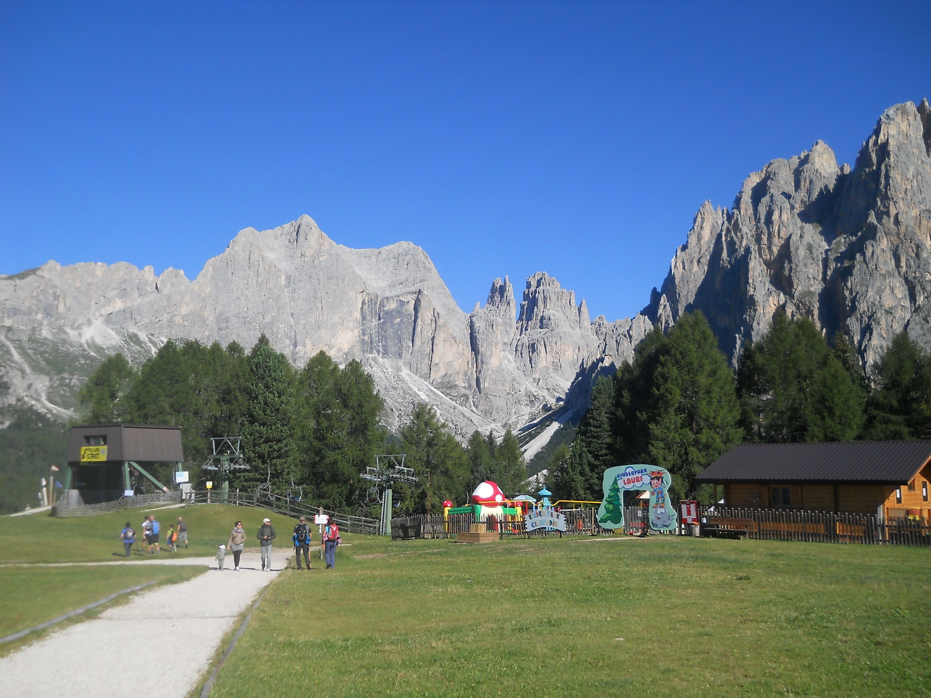 Paisagem montanhosa com um teleférico, um chalé de madeira e uma placa para Kinderpark Lauri.