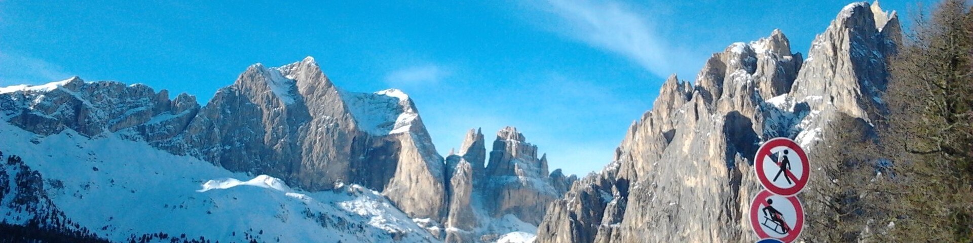 Paisagem de montanha com picos cobertos de neve, céu azul límpido e um sinalizador com informações de direção.