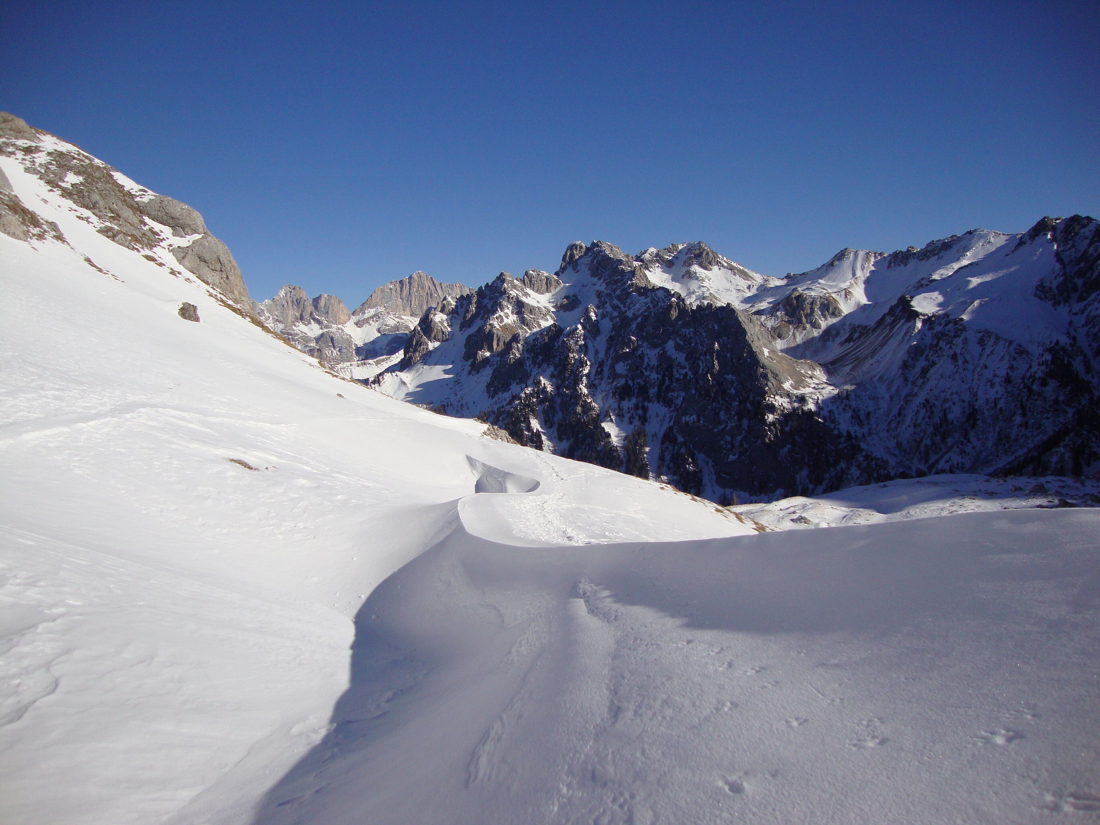 Encosta de montanha coberta de neve, com afloramentos rochosos e um céu azul límpido.