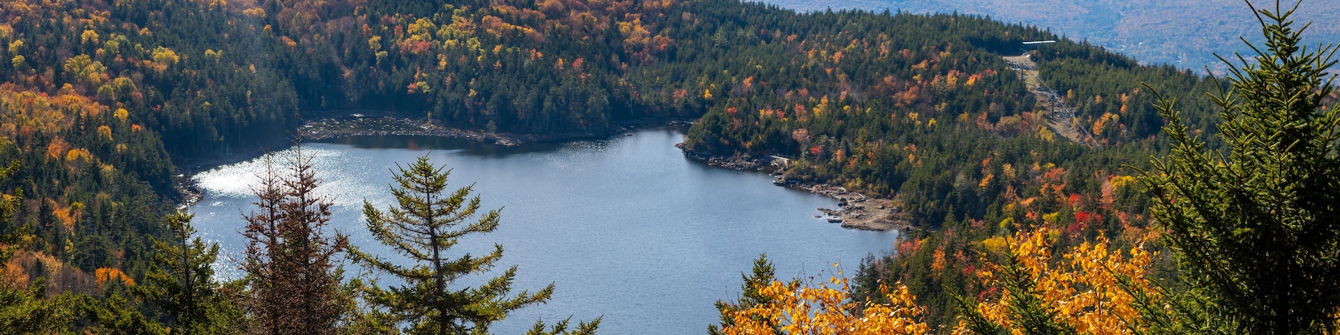 Um lago rodeado por árvores com cores de outono e uma paisagem montanhosa.