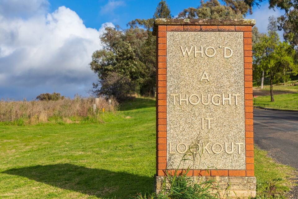 Um letreiro com o texto 'WHO'D A THOUGHT I LOOKOUT' em um ambiente rural.