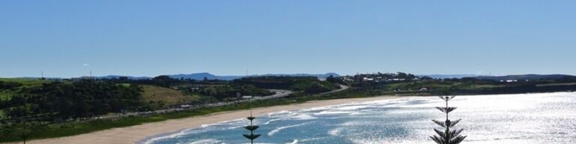 Paisagem costeira com uma praia de areia, um rio ou estuário e árvores de coníferas.