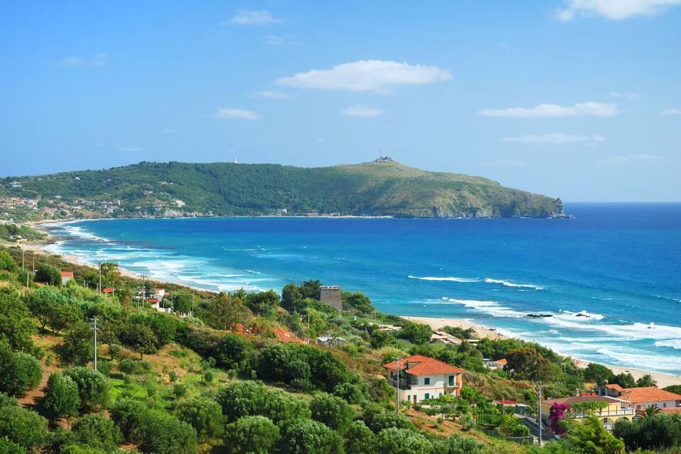 Paisagem costeira com uma colina, oceano e edifícios residenciais.