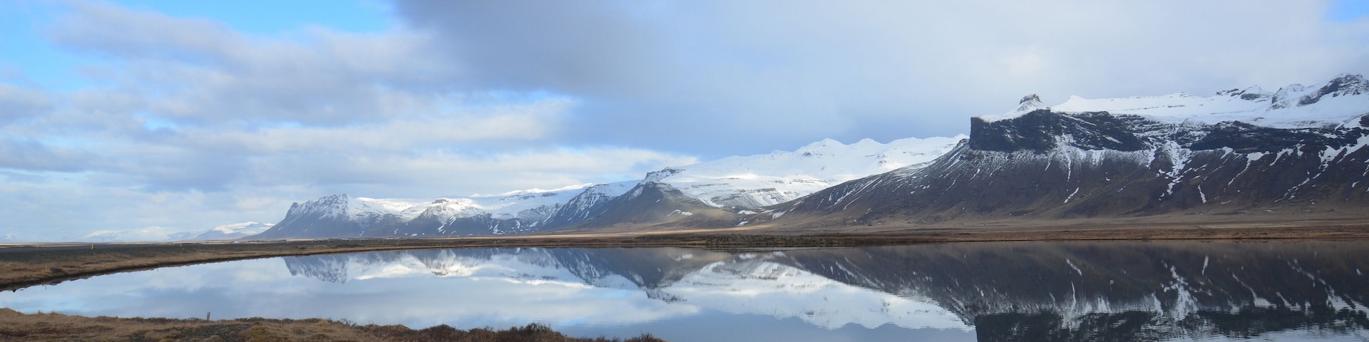 Cordilheira com picos nevados refletidos em um lago calmo.