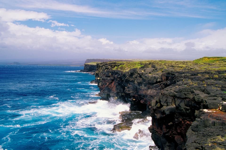 Paisagem costeira com um penhasco rochoso, ondas do oceano e céu claro.