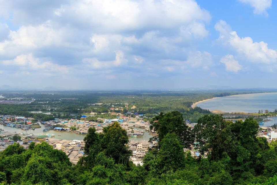 Uma cidade costeira com rio, vegetação densa e uma ponte.