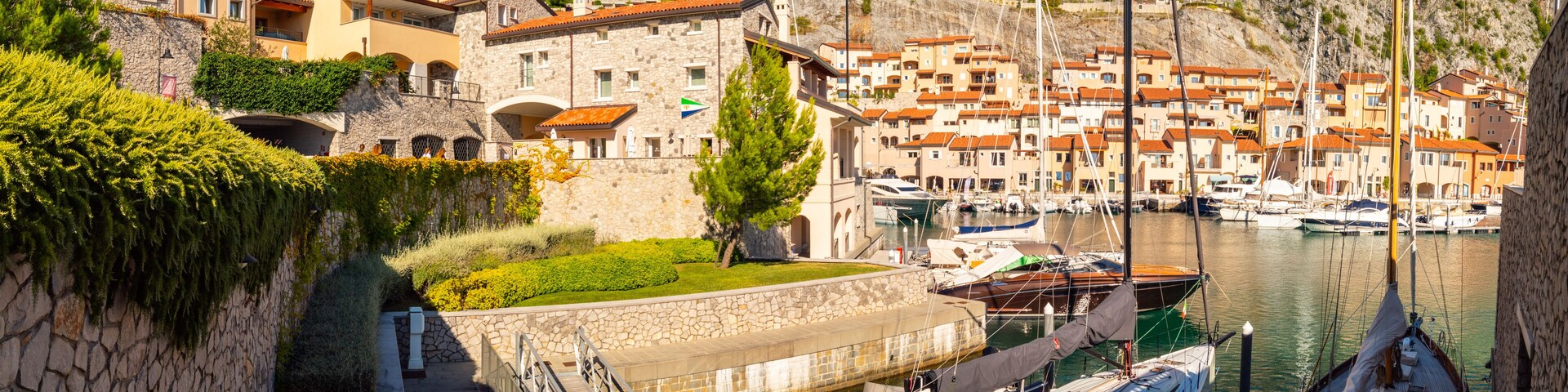 Uma vila costeira com edifícios de pedra, um porto e barcos atracados.