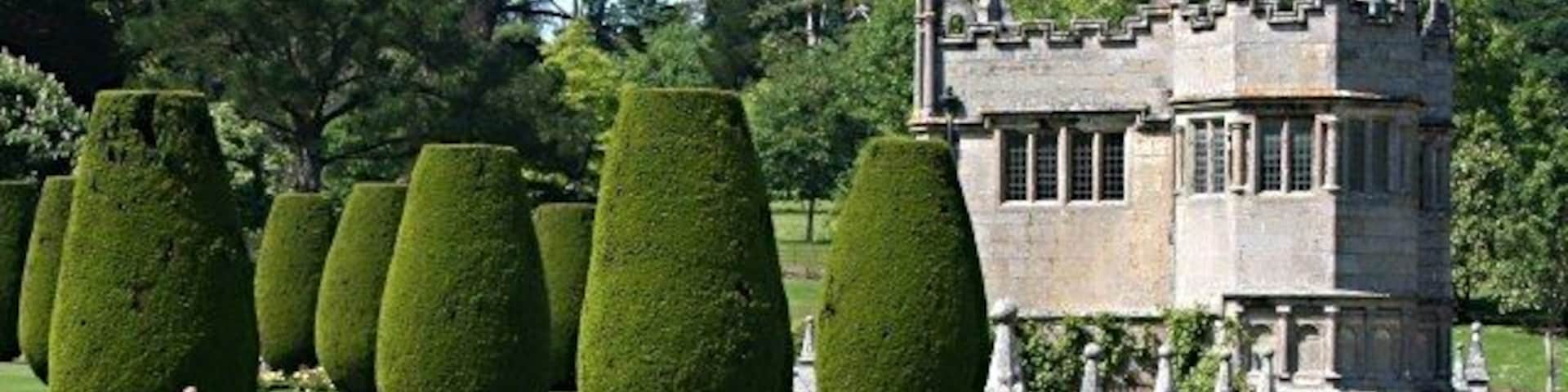 Um edifício histórico de pedra com fachada simétrica, rodeado por um jardim bem cuidado.