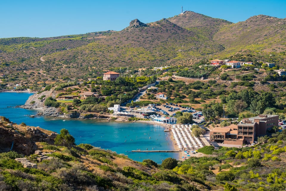 Uma vila costeira com casas numa encosta, uma praia e um mar azul límpido.
