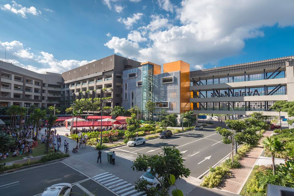 Uma praça urbana moderna com passagem para pedestres, área de estacionamento e edifícios comerciais e residenciais.
