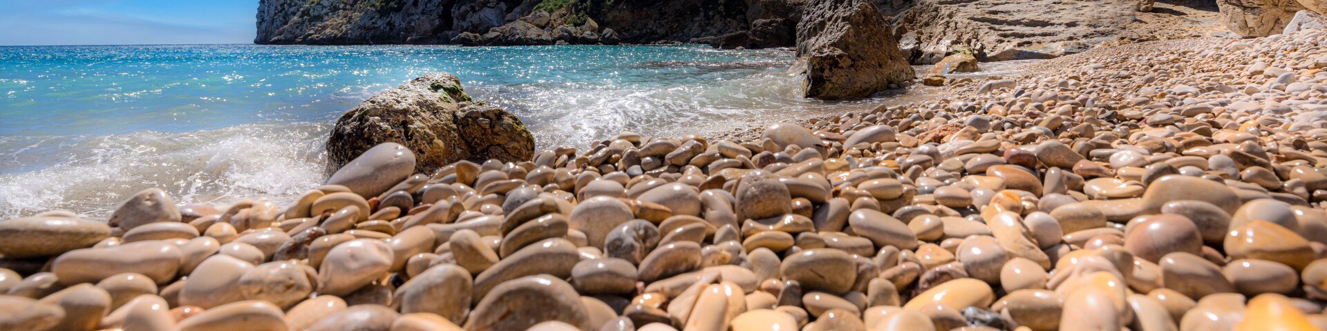 Uma praia de pedras com água turquesa translúcida e falésias rochosas.