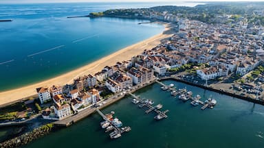 Vista aérea de uma vila costeira com marina, praia e área urbana densa.