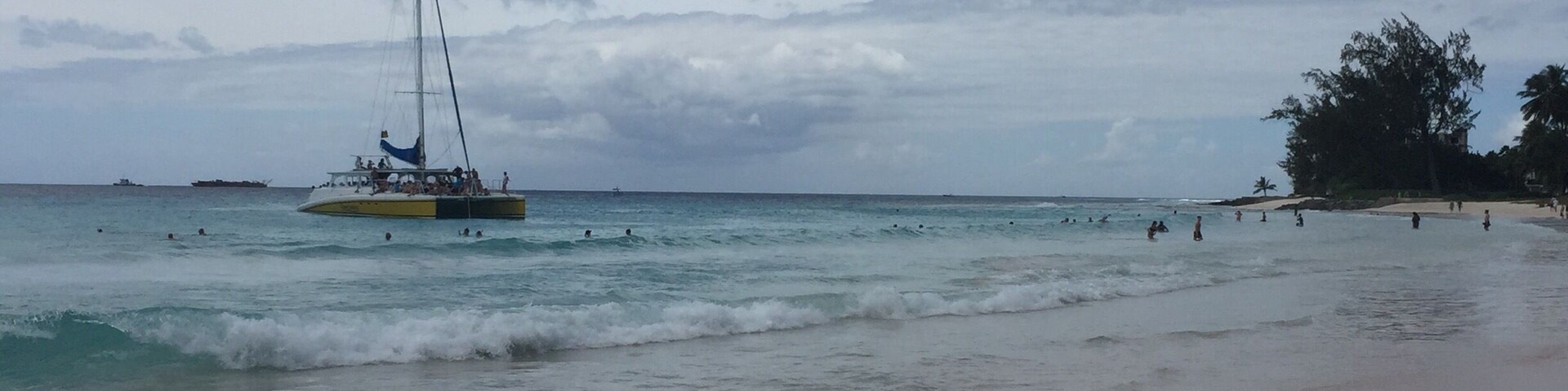 Uma praia com um veleiro na água e pessoas nadando.