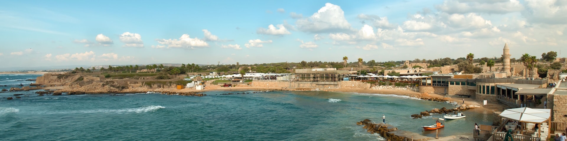 Uma vila costeira com costas rochosas, uma praia e uma torre histórica.