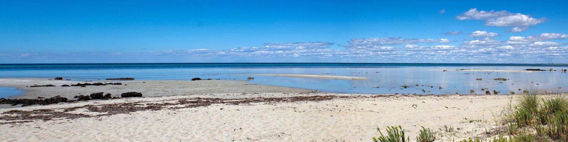 Uma praia de areia com águas azul-claras e pedras espalhadas.