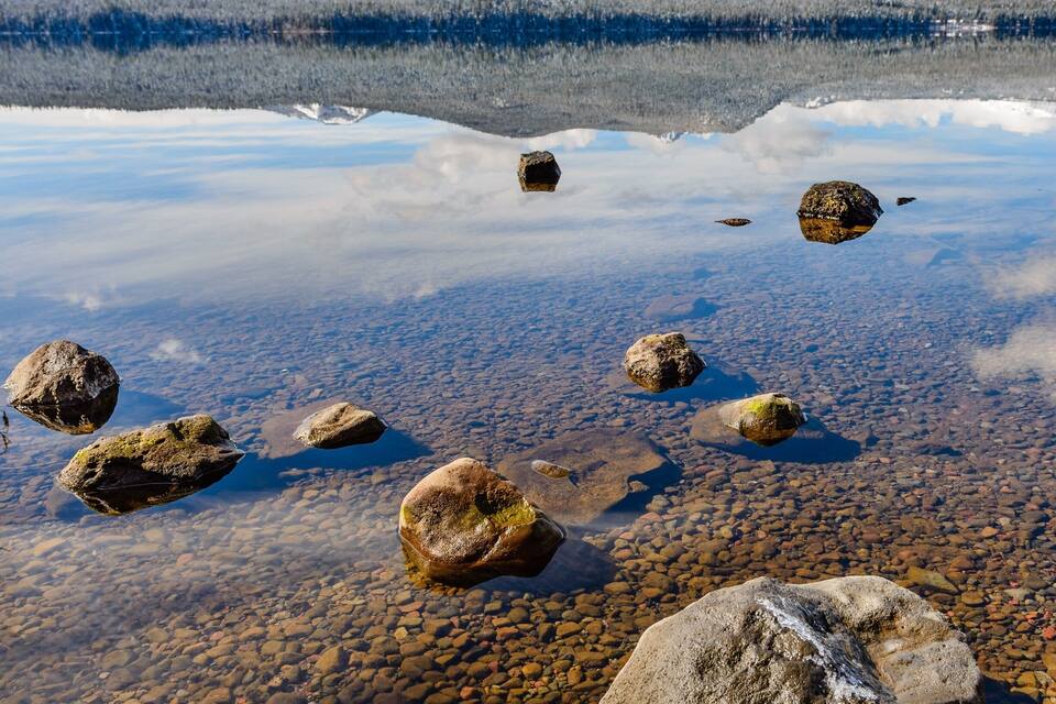 Um lago límpido com rochas visíveis e uma montanha ao fundo.