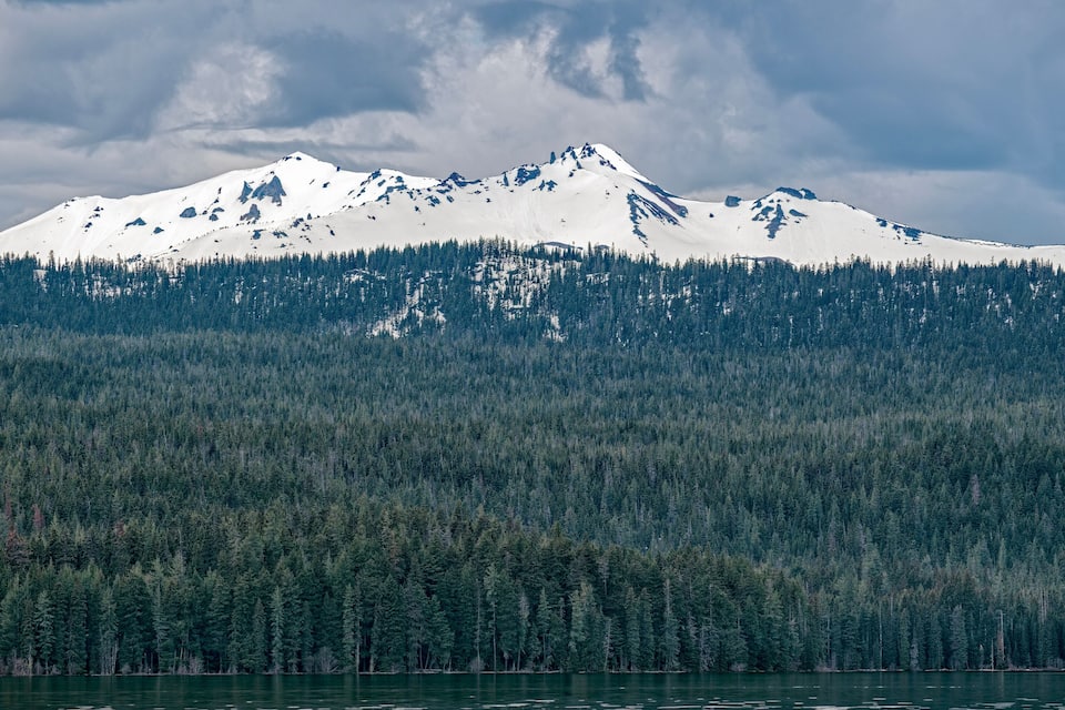 Montanha coberta de neve, floresta densa e um lago.