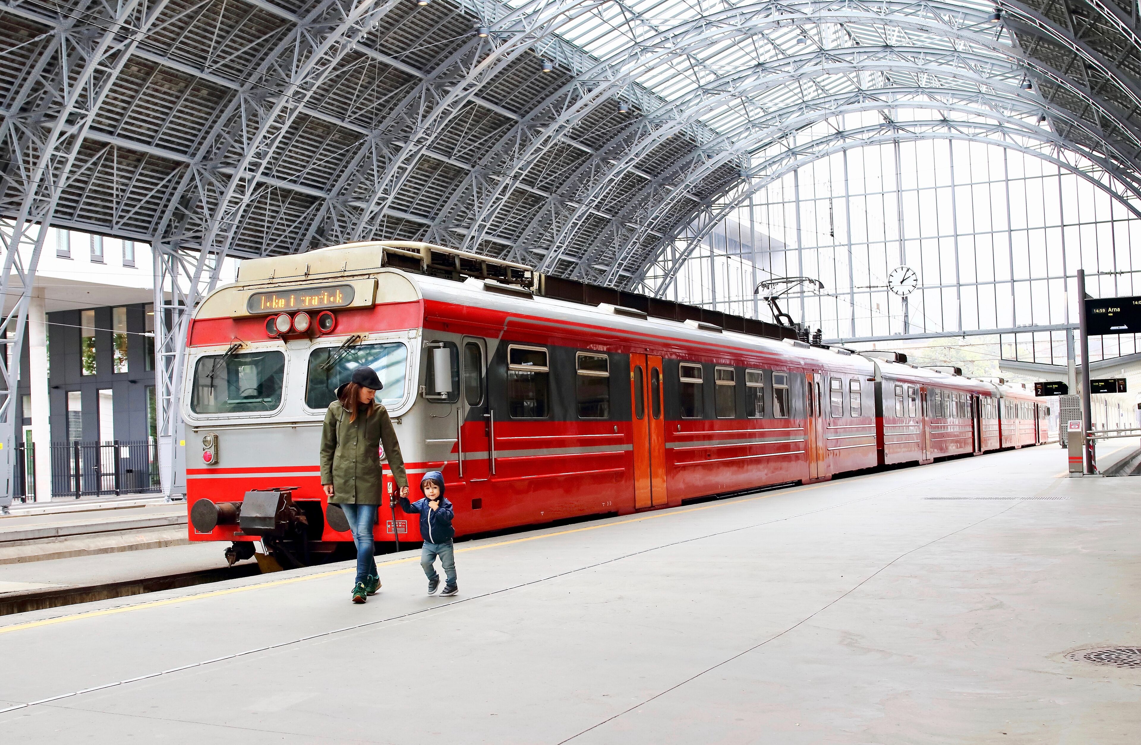 Um trem vermelho em uma estação com telhado de metal e um relógio.