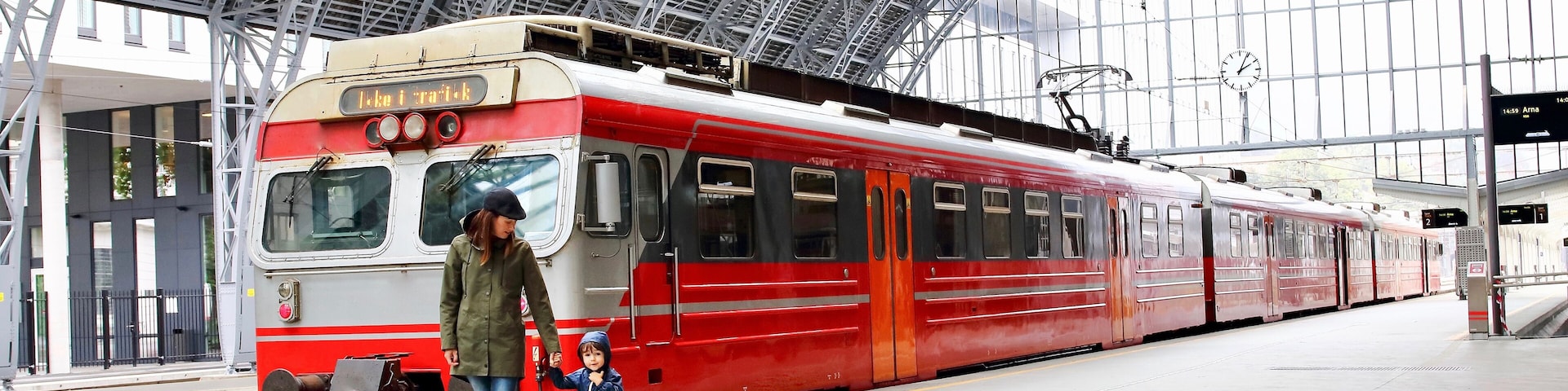 Um trem vermelho em uma estação com telhado de metal e um relógio.