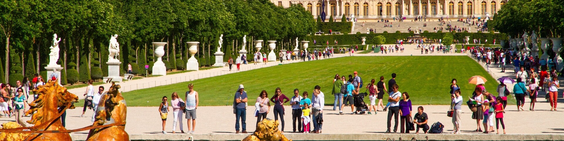 Grande multidão em um palácio histórico com uma fonte de bronze com cavalos.