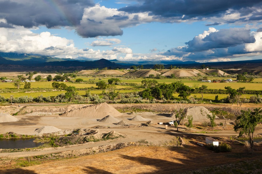 Paisagem rural com colinas onduladas, estrada de terra e construções dispersas.