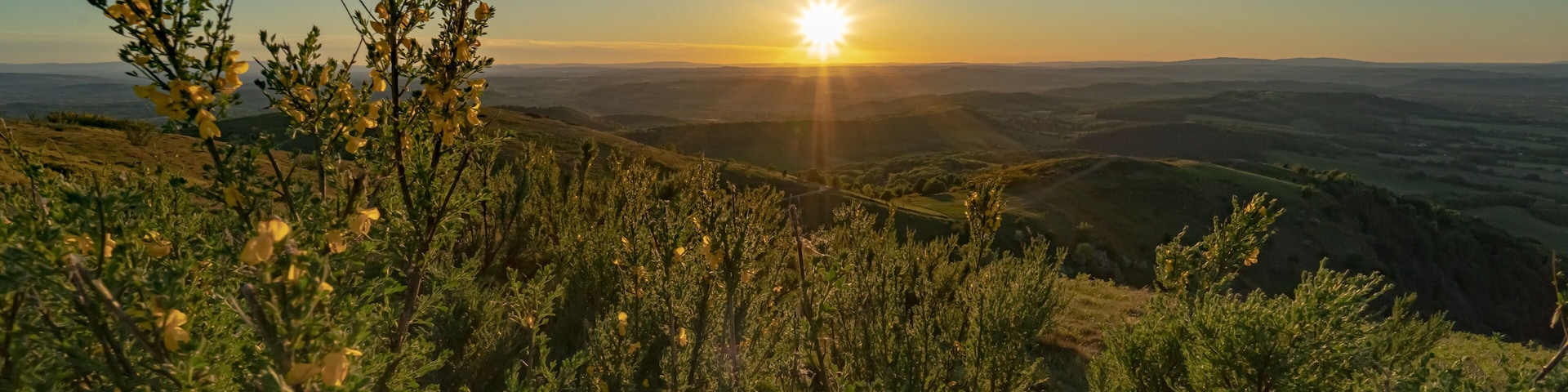 Pôr do sol sobre colinas ondulantes com vegetação escassa.