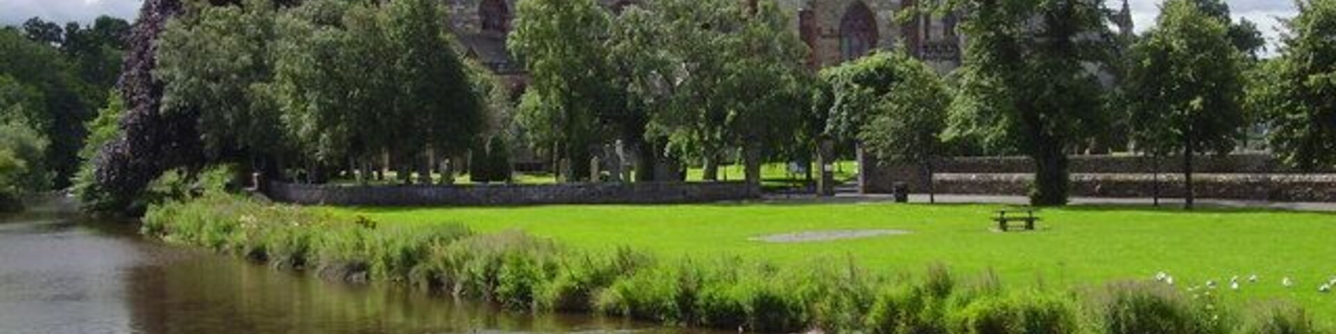 Um edifício histórico com uma torre, rodeado por um lago e vegetação exuberante.