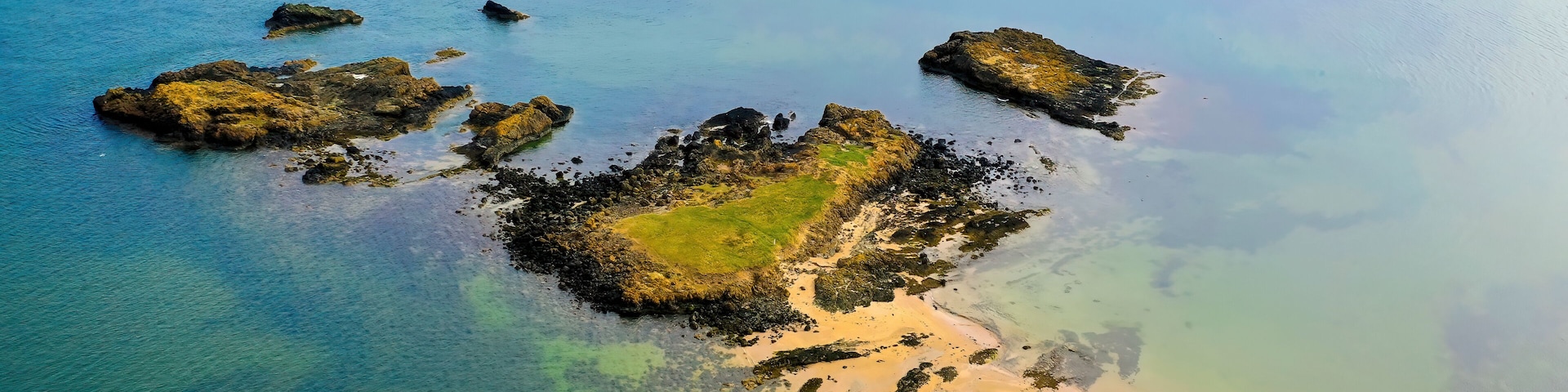 Paisagem costeira com águas cristalinas, afloramentos rochosos e uma praia de areia.