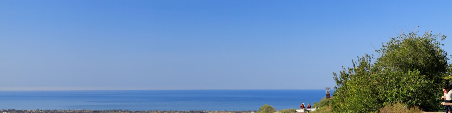 Paisagem costeira com céu claro, um caminho de terra e vista para o mar.