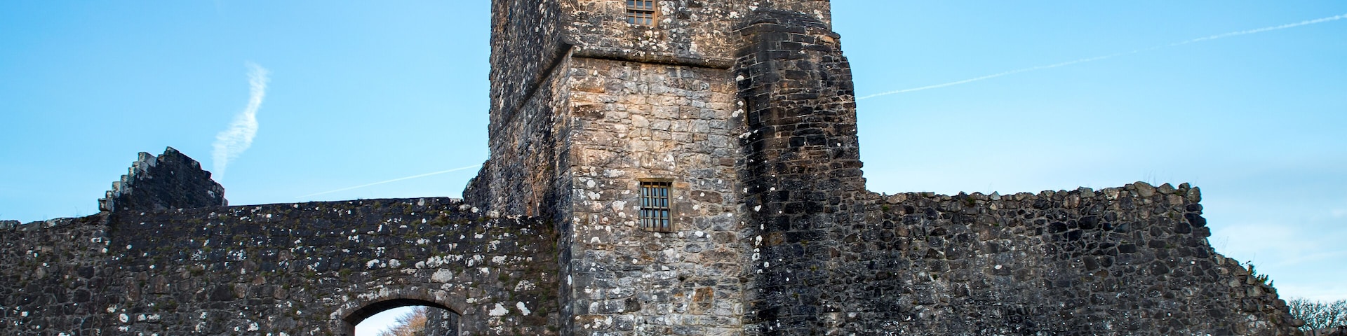 Uma torre de pedra histórica com uma grande entrada em arco, cercada por gramado e um caminho de cascalho.