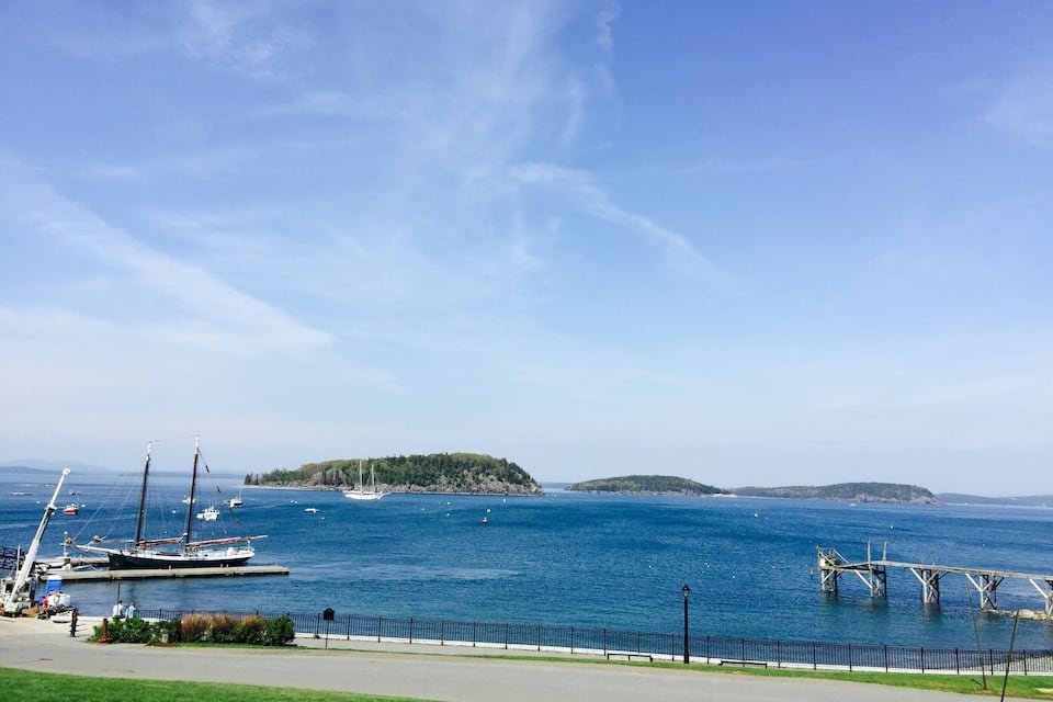 Um porto costeiro com barcos, um cais e uma área gramada em primeiro plano.