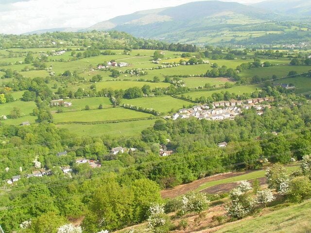 Paisagem rural com colinas ondulantes, casas dispersas e campos.