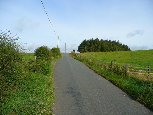 Uma estrada rural ladeada por campos verdes e uma cerca de madeira.