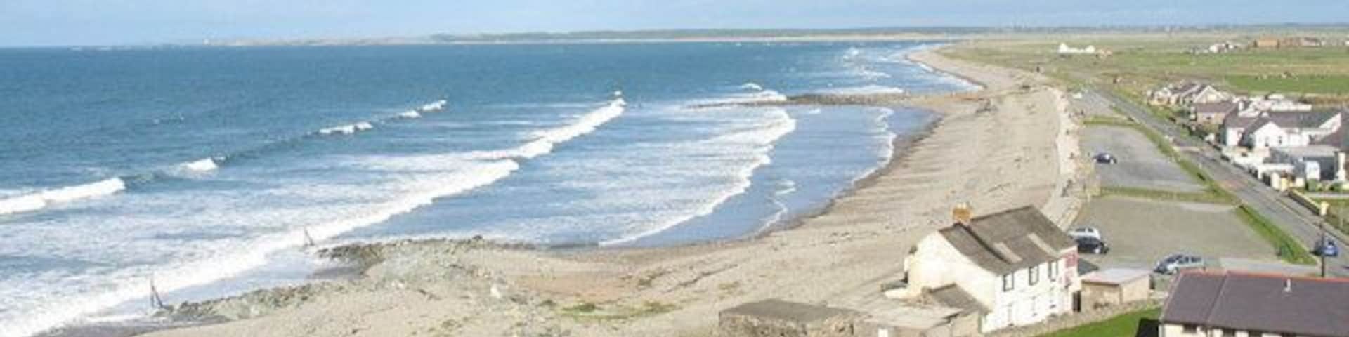 Dinas Dinlle Village from Dinas Dinlle Dinas Dinlle Village is dominated by Dinas Dinlle - an Iron Age fort. This view is taken from the ramparts of that fort. It shows the beach, which has gained the Blue Flag Award, and which consists of pebbles at the top and fine sand lower down (here hidden by the high tide). It is a popular venue for wind surfing. There are several cafes and shops in the village.