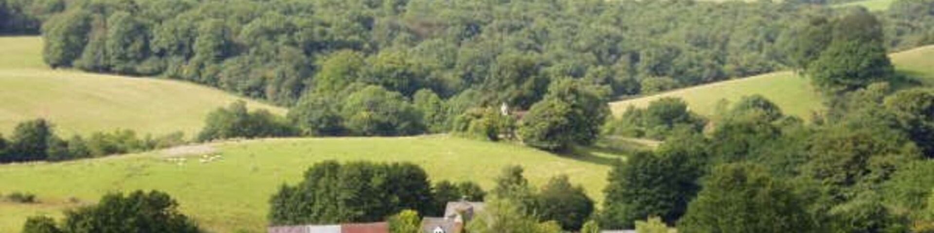 Colinas verdes ondulantes, um celeiro vermelho e uma casa pequena numa paisagem rural.