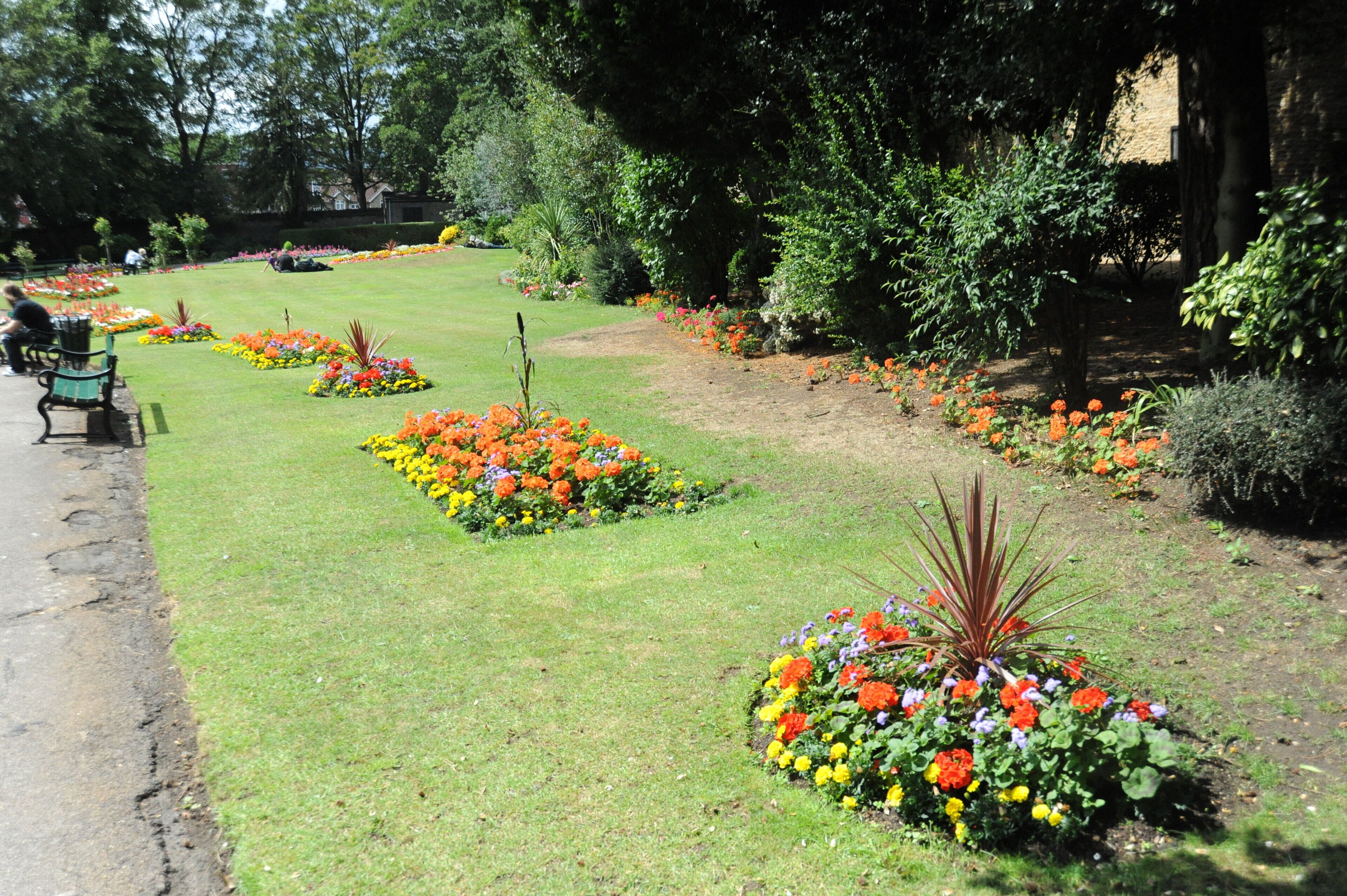 Um jardim bem cuidado com vários canteiros de flores e um banco ao longo de um caminho.