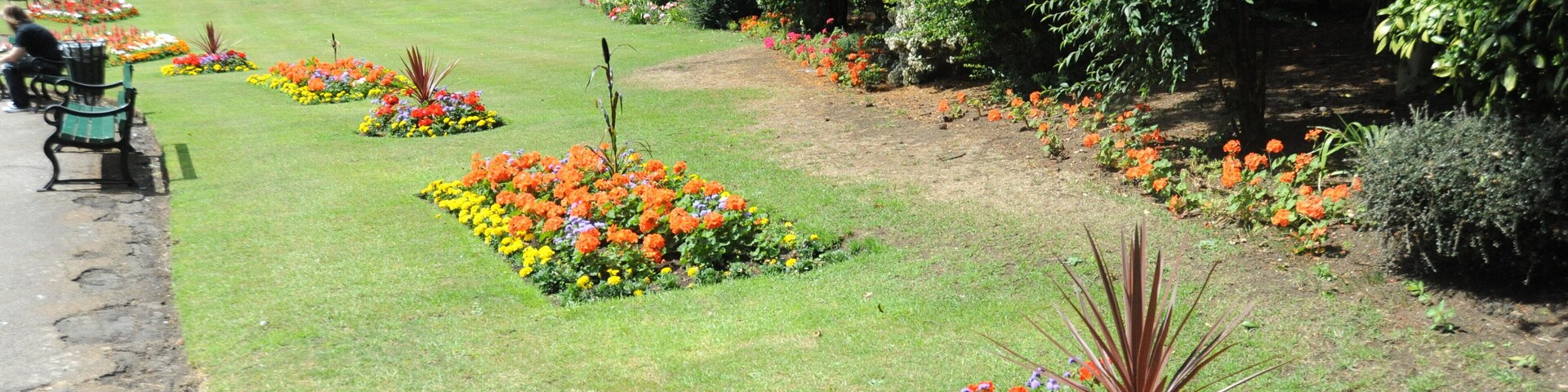 Um jardim bem cuidado com vários canteiros de flores e um banco ao longo de um caminho.