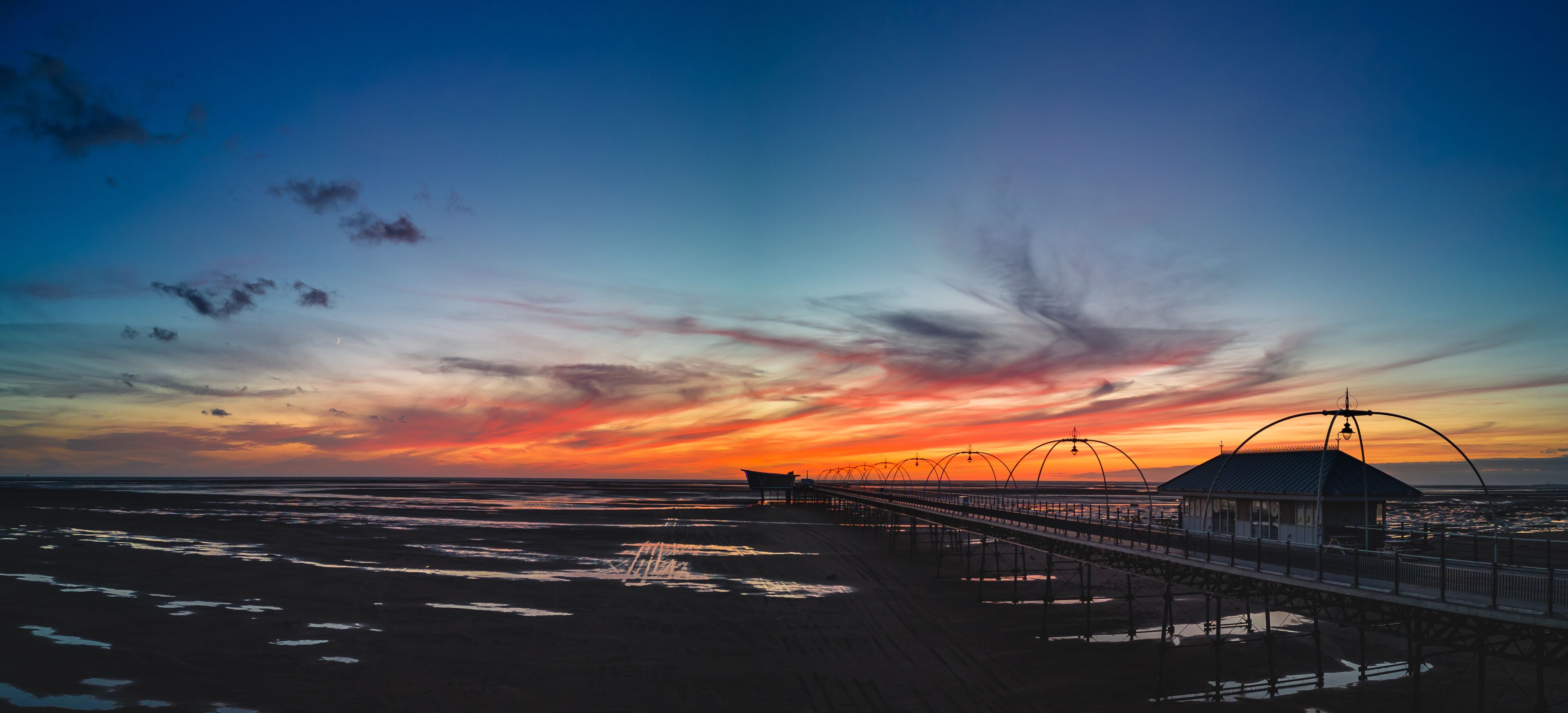 Um pôr do sol sobre uma praia com um cais e um edifício.