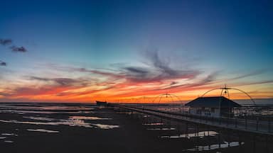 Um pôr do sol sobre uma praia com um cais e um edifício.
