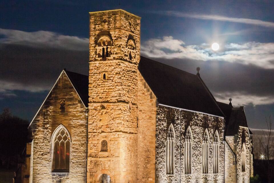 Uma igreja de pedra com uma torre e janelas em arco à noite.