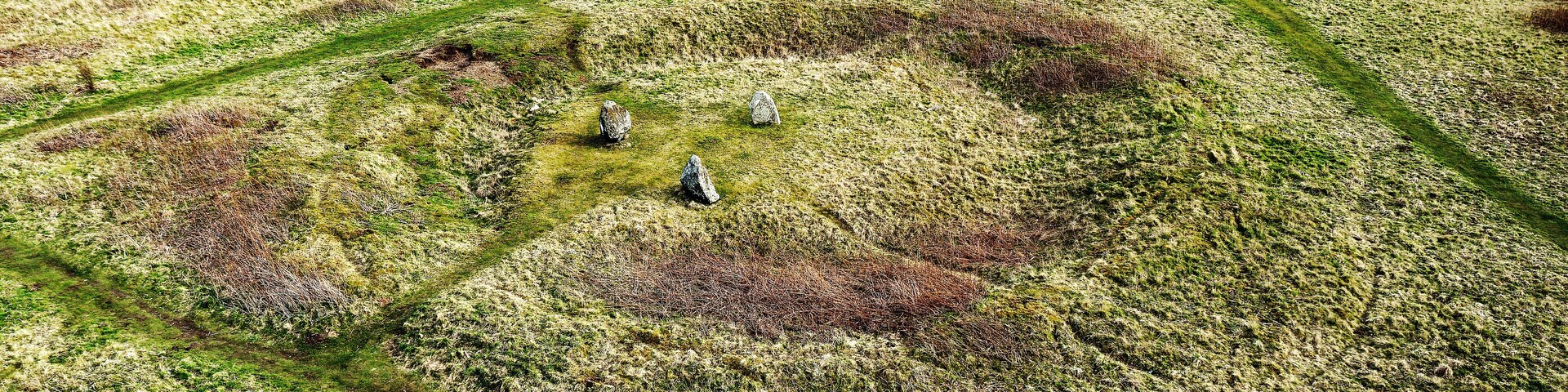 Um campo gramado com padrões geométricos bem definidos e várias pedras verticais.