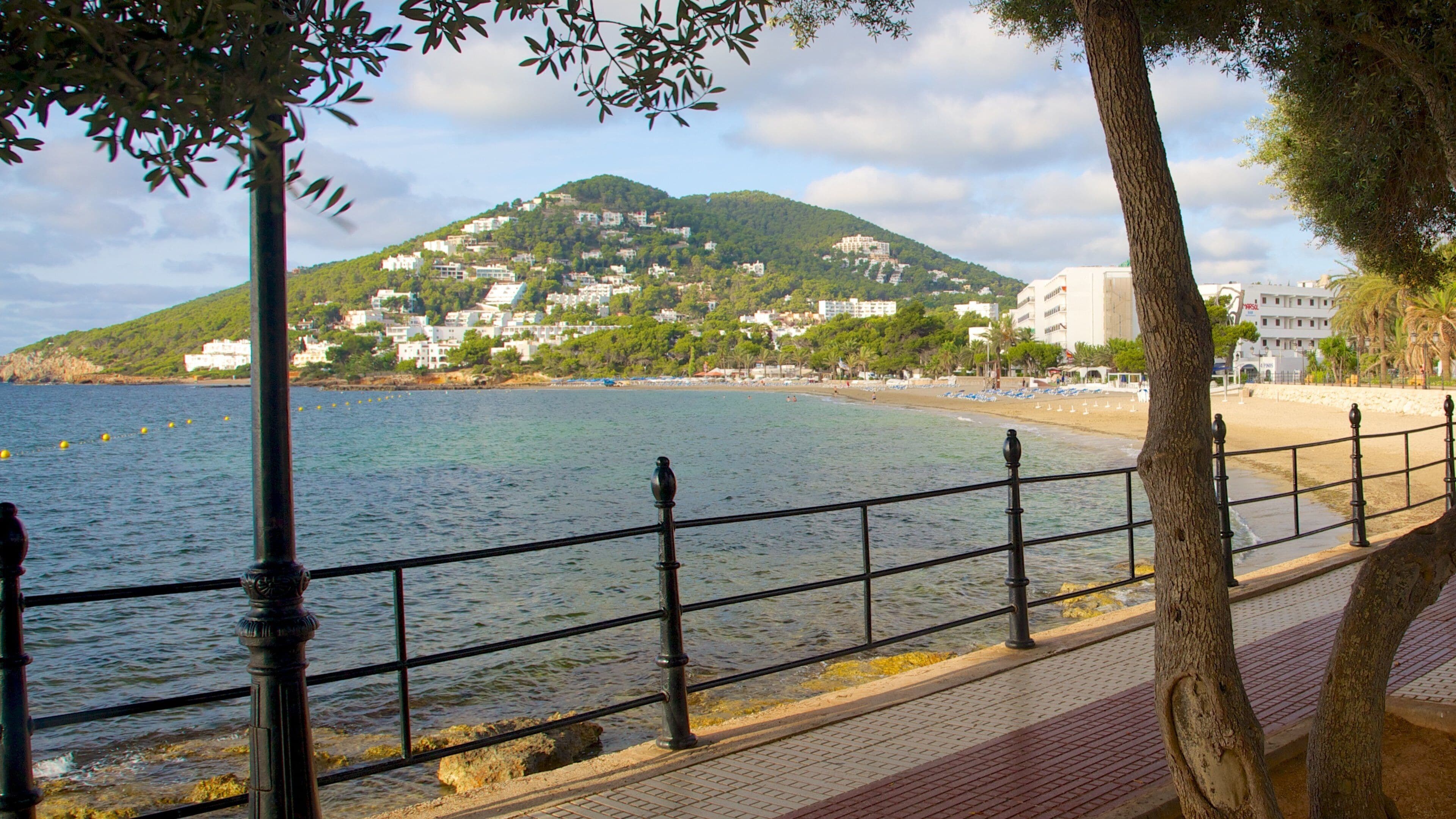 Uma vila costeira com uma praia, um calçadão e uma colina com edifícios.