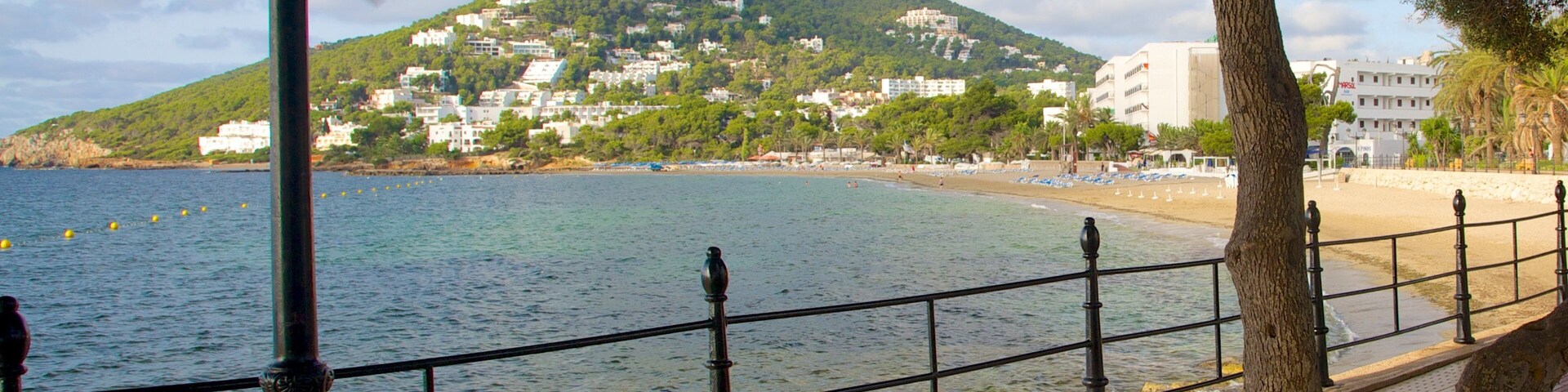 Uma vila costeira com uma praia, um calçadão e uma colina com edifícios.