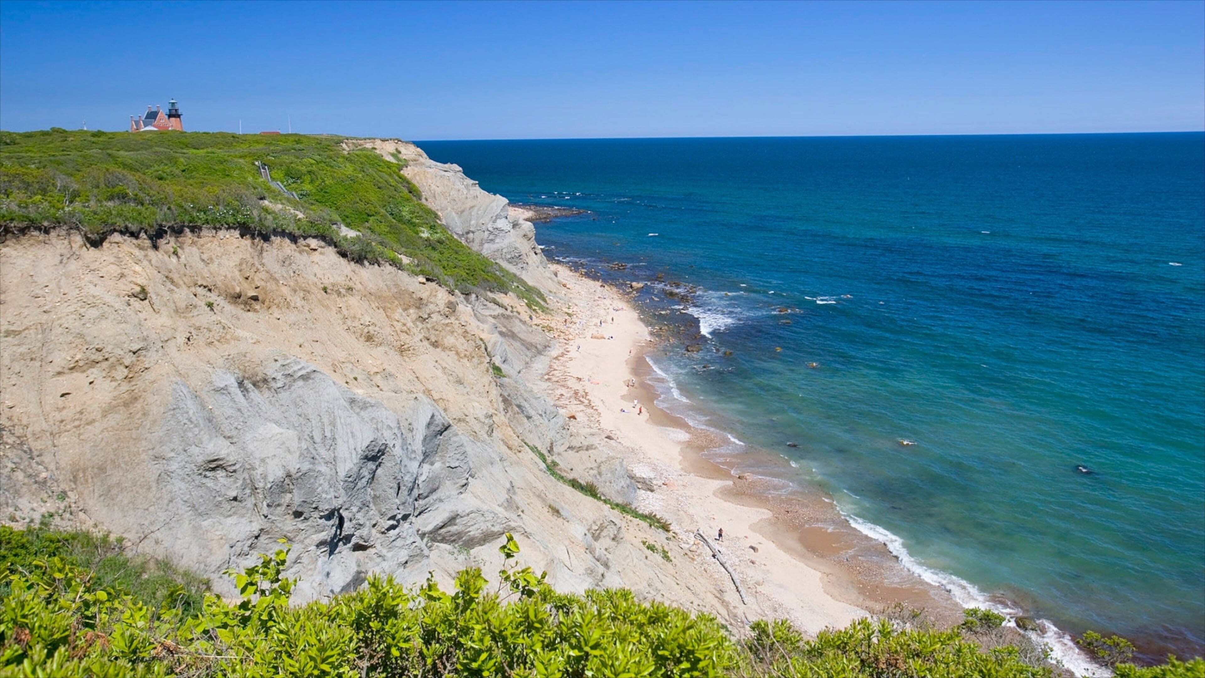 Um penhasco costeiro com um farol, praia e oceano.