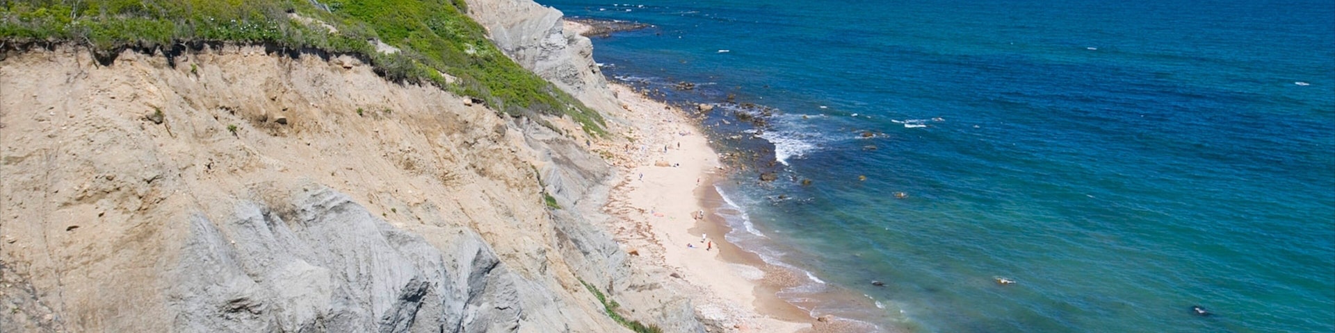 Um penhasco costeiro com um farol, praia e oceano.